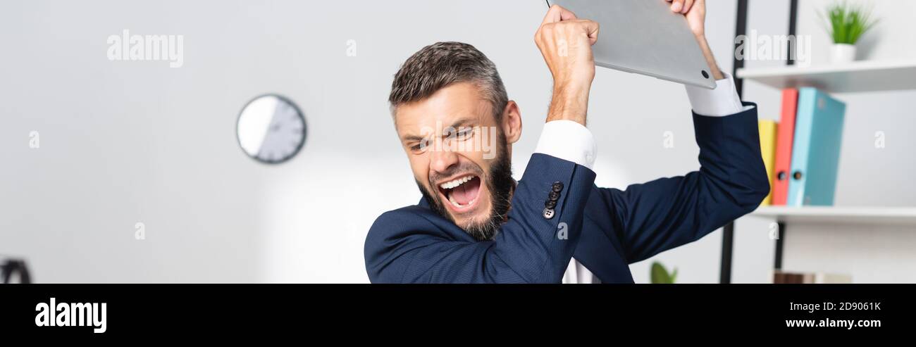 Angry businessman holding laptop while screaming in office, banner ...