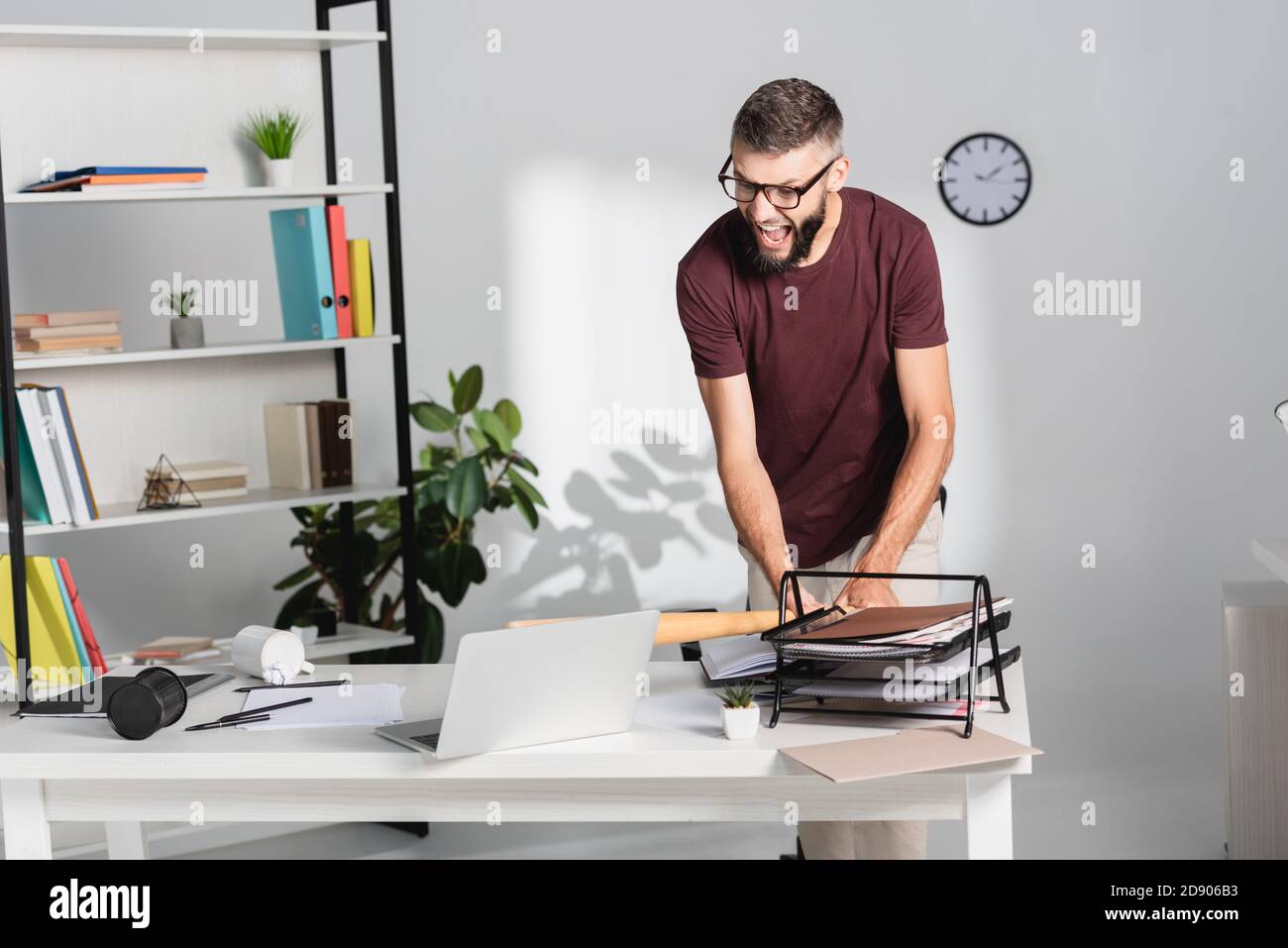 Angry businessman beating laptop with baseball bat near stationery on ...