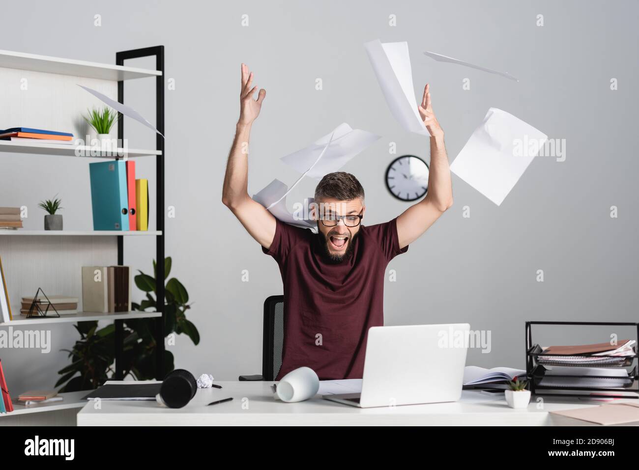 Stressed businessman screaming while throwing papers near laptop on ...