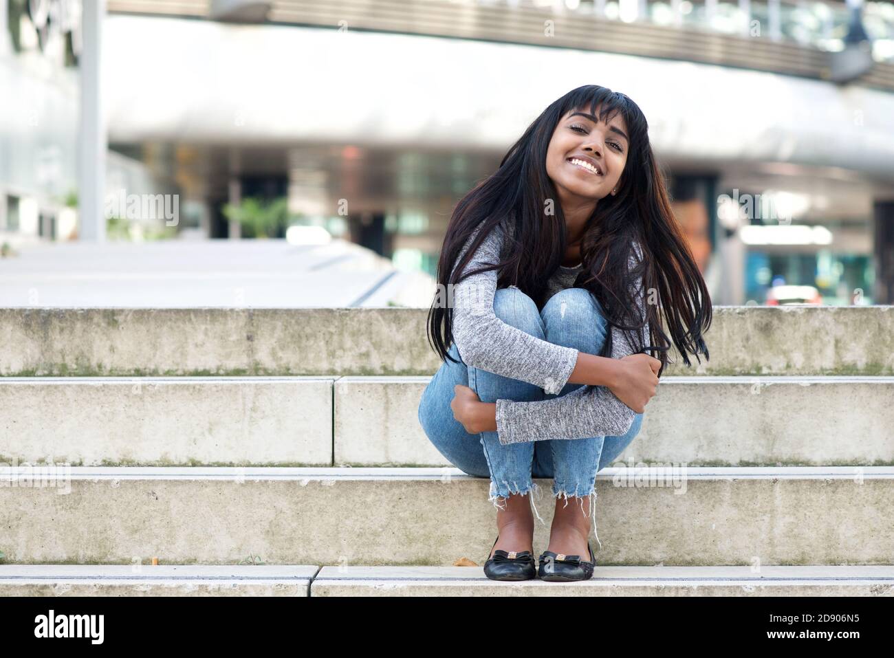 Full body front portrait of smiling young Indian woman sitting on steps ...