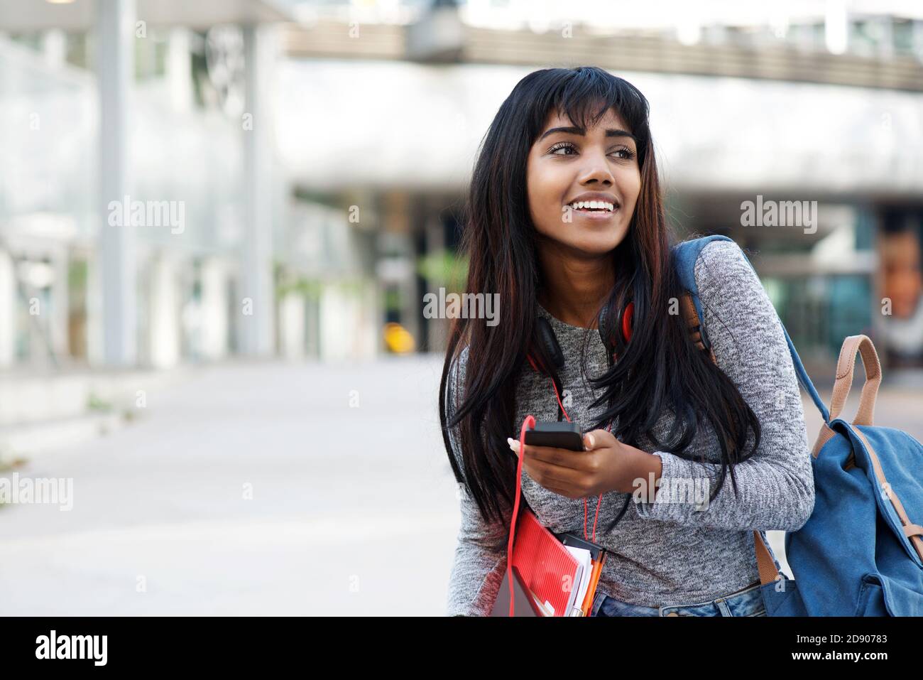 Portrait of happy Indian university student walking with mobile phone ...
