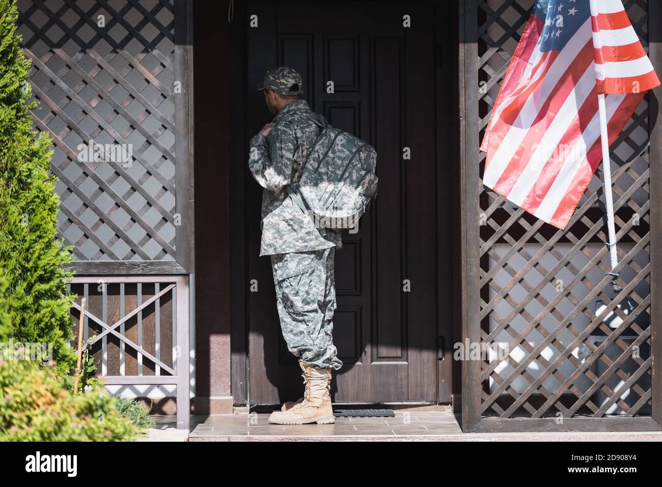 Back view of military man with backpack standing near house door and ...