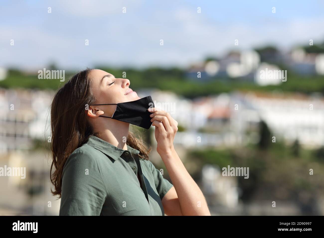 Relaxed woman taking off mask breathing fresh air in a town on vacation ...