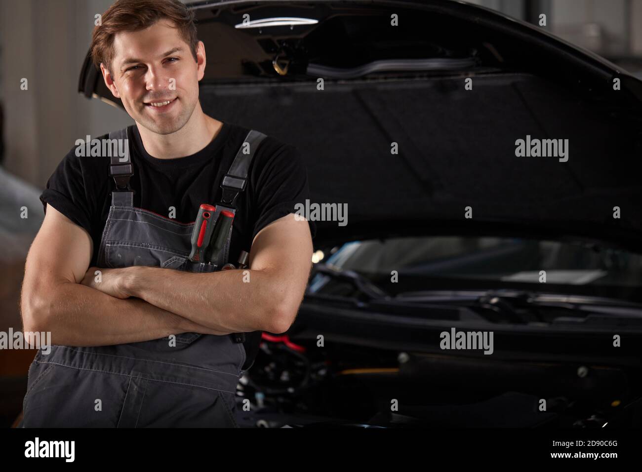 portrait of handsome caucasian auto mechanic man, standing near the car ...