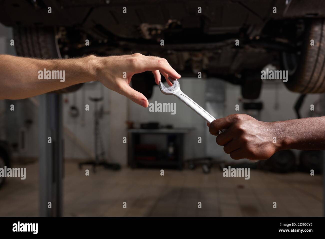 two young diverse mechanics hands giving, sharing tool to each other ...