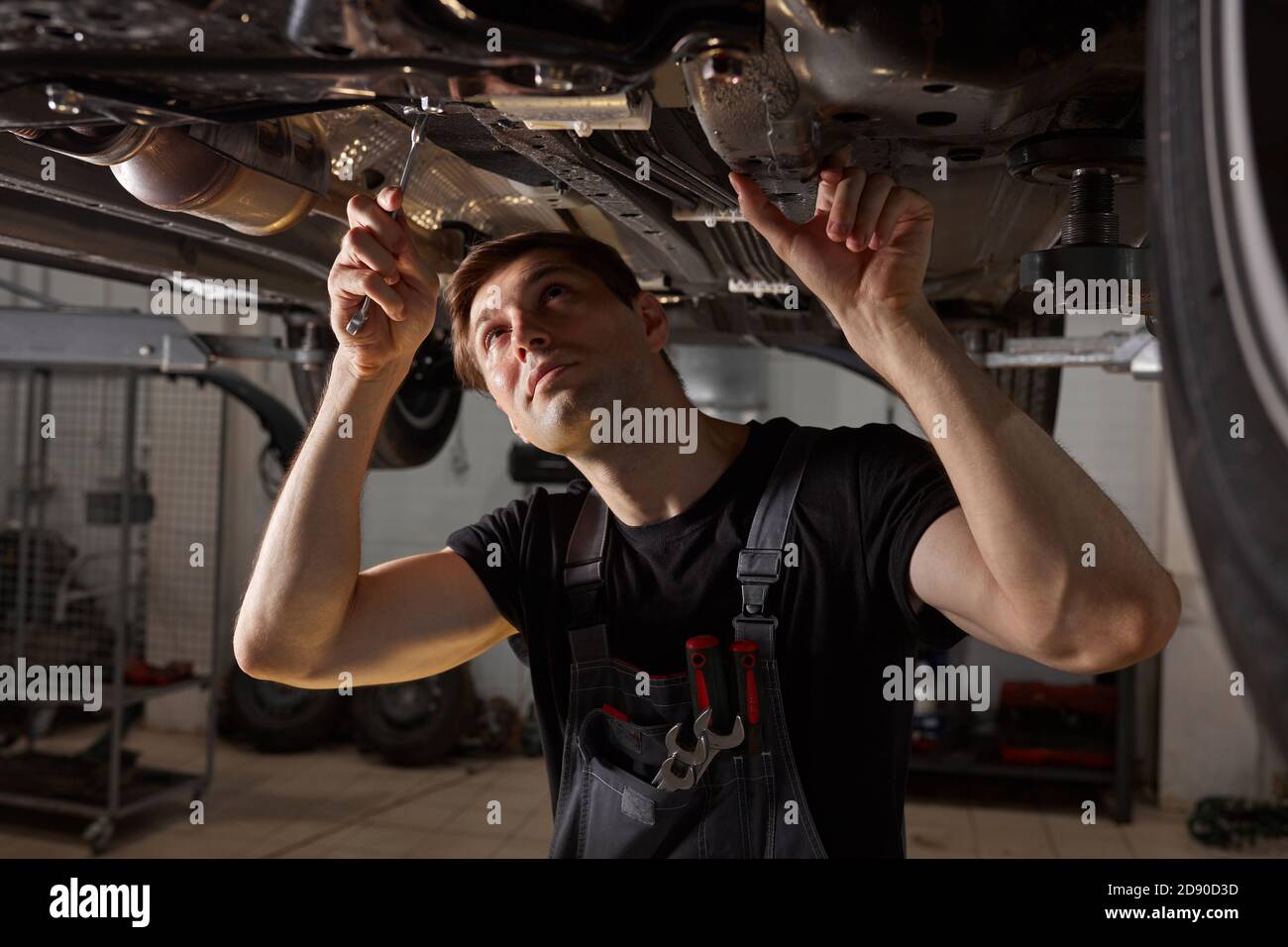 young male car mechanic in uniform checking car in automobile service ...