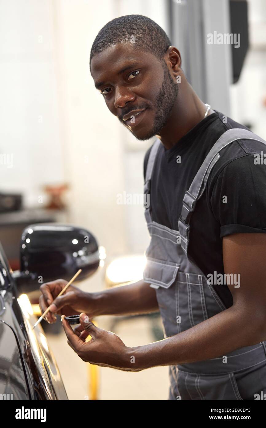 confident auto mechanic man using brush for painting a car, applying ...