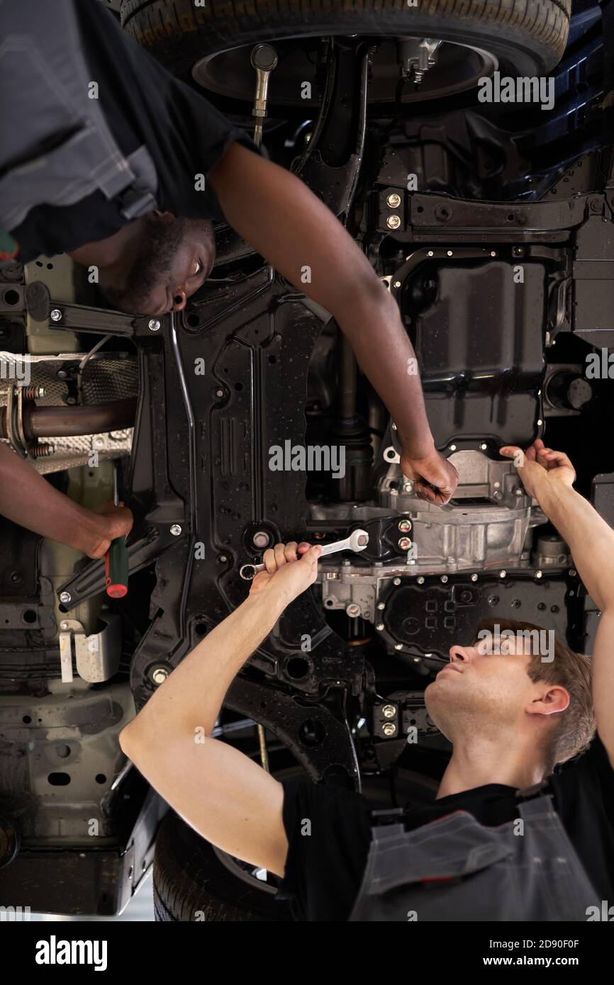 two mixed race auto mechanic males have successful work together, they ...