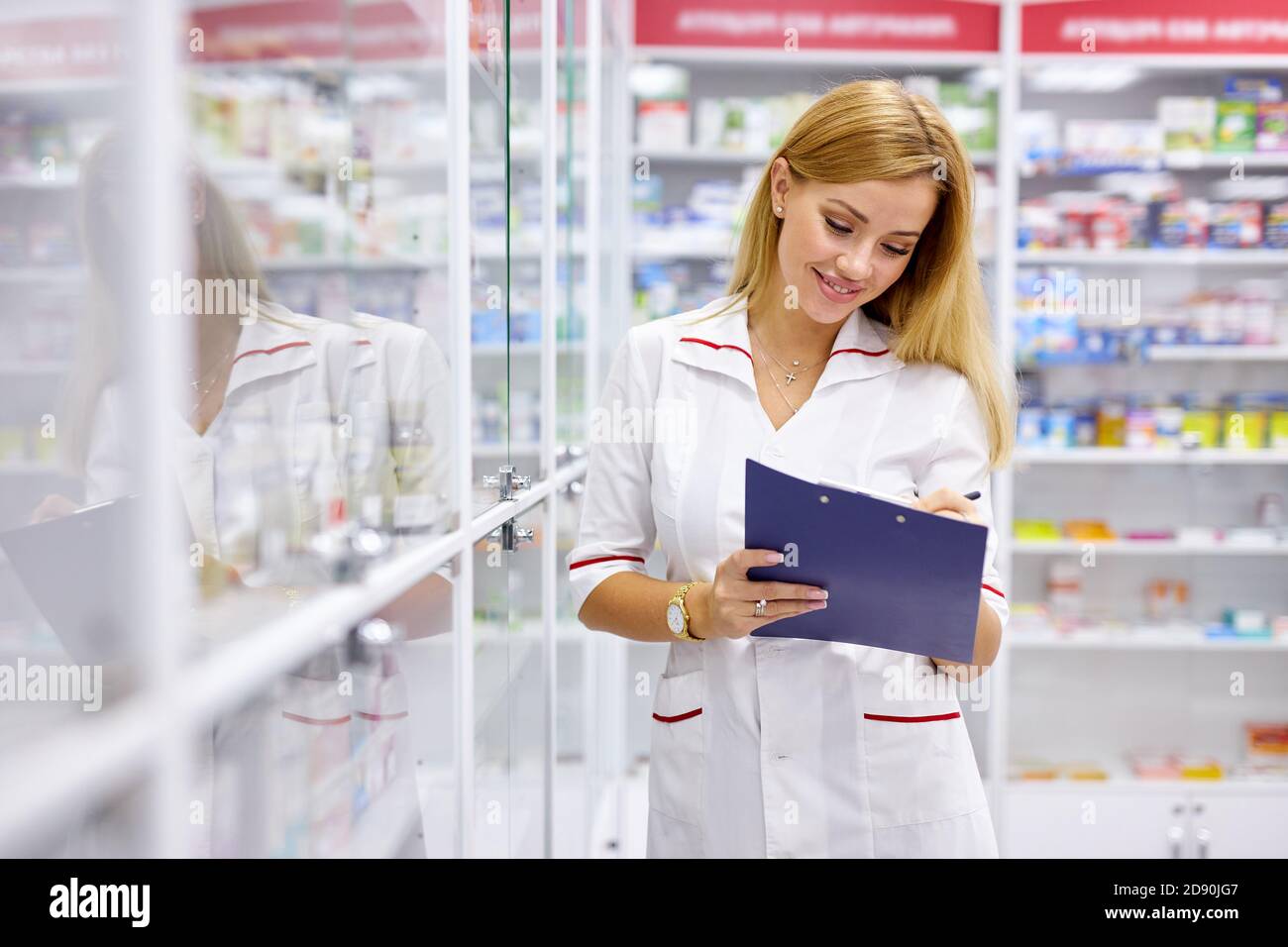 portrait of good-looking blonde pleasant female pharmacist writing on ...