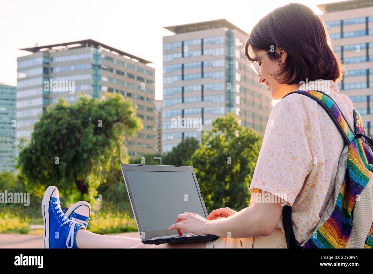 rear view of a young woman working in the city with her laptop and ...