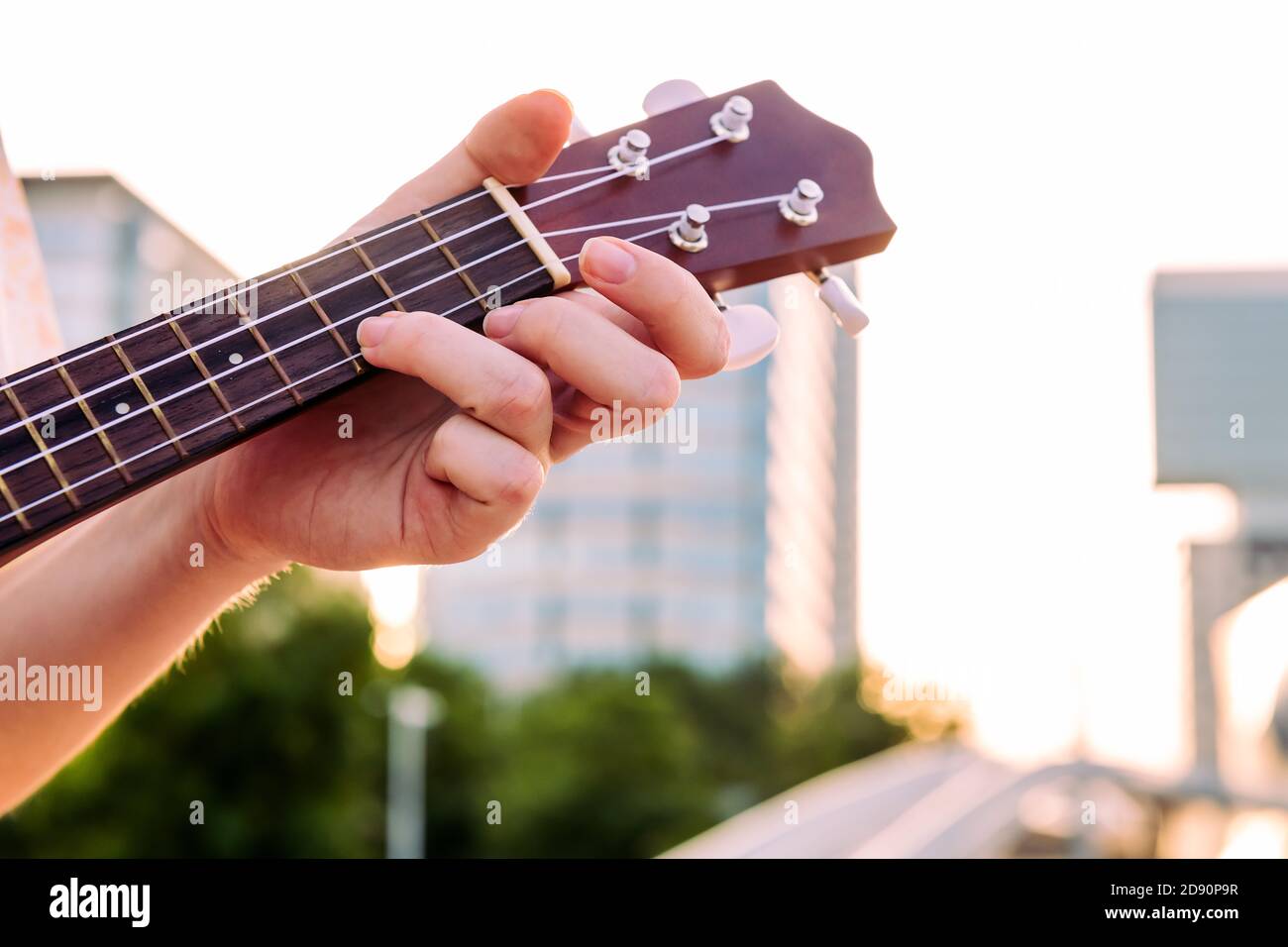 close-up of a woman's hand on the neck of a ukulele at sunset in the ...