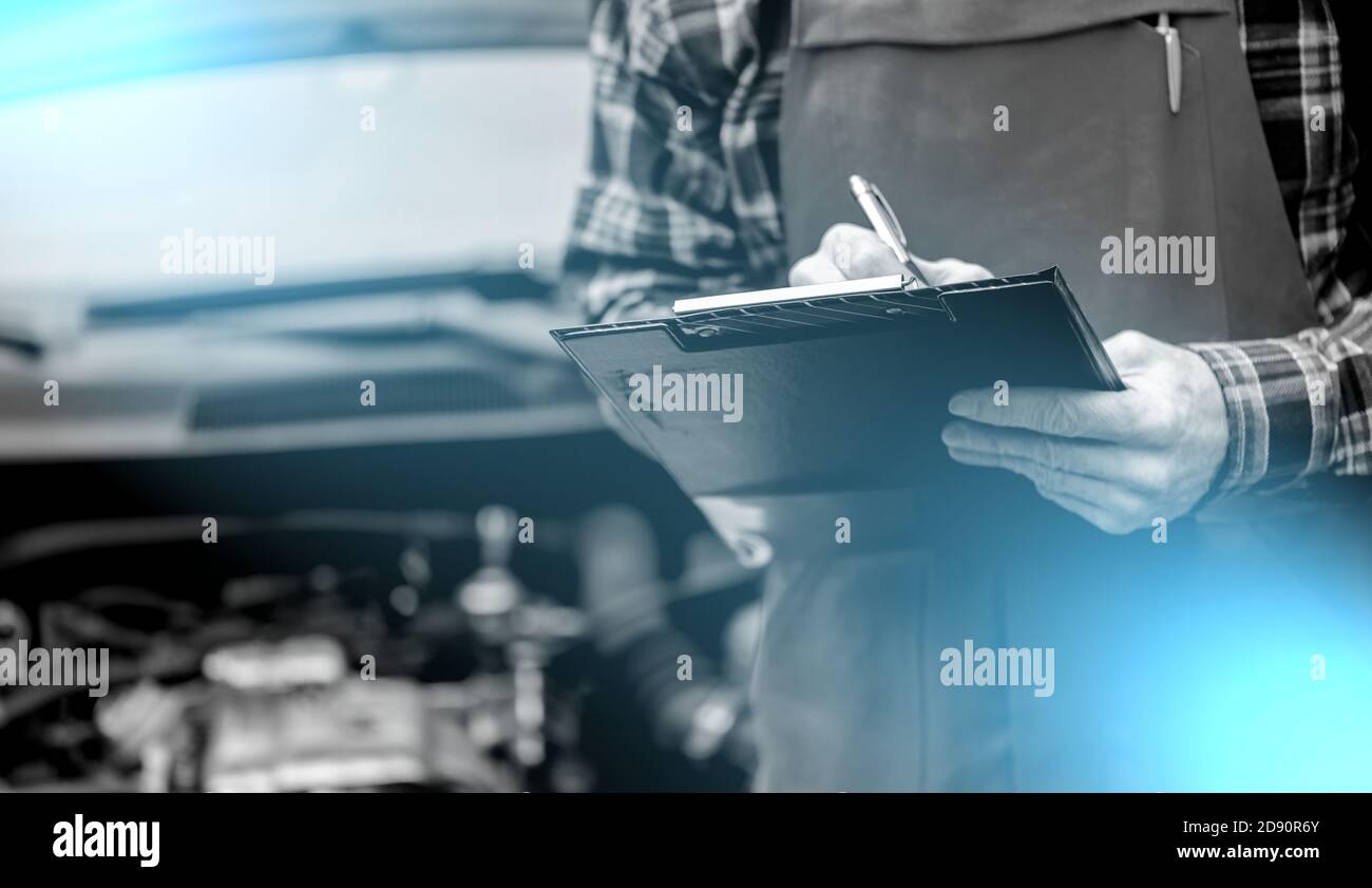 Car mechanic checking a car engine and writing on clipboard; light ...