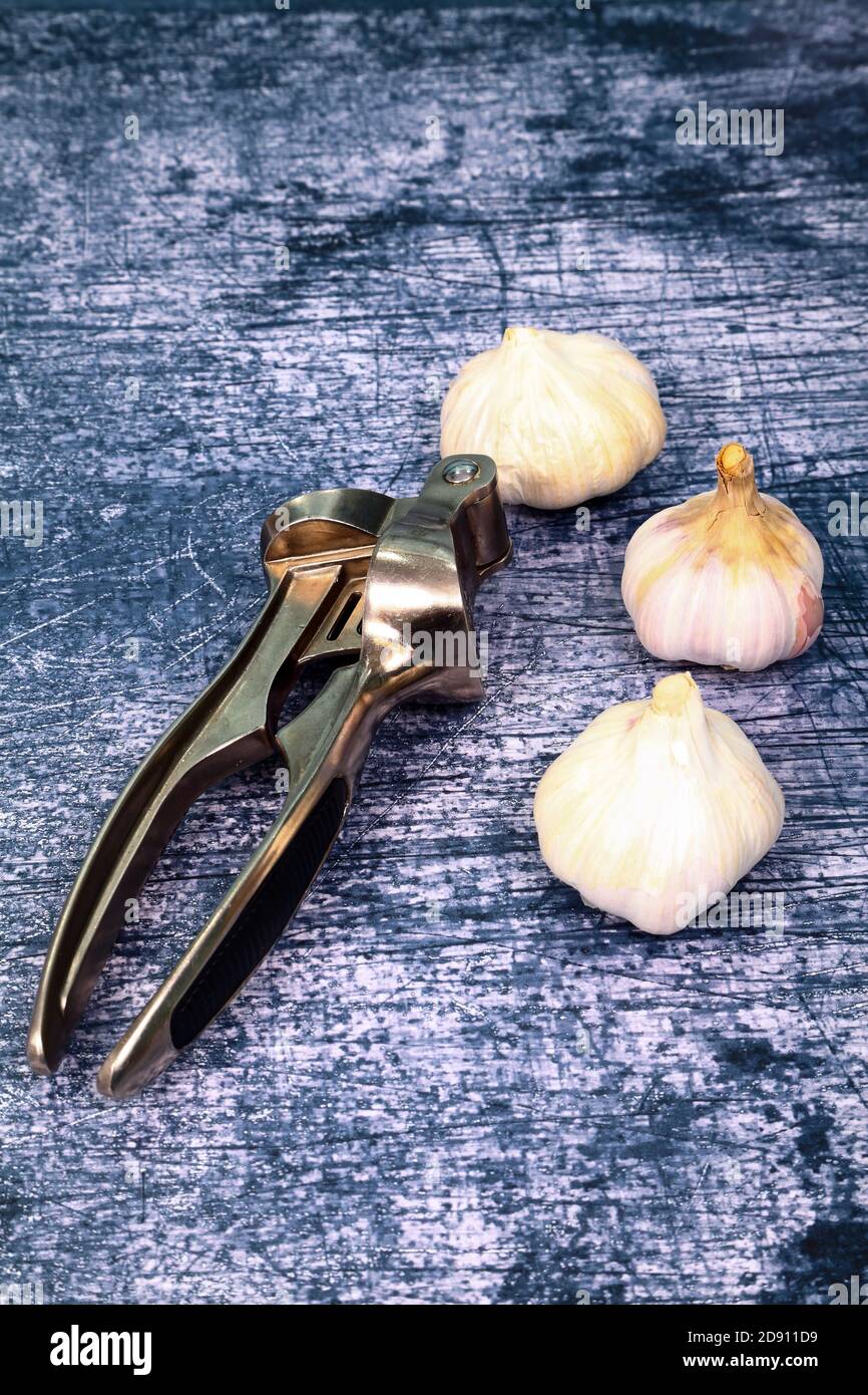 Three garlic bulbs and a press on a textured background Stock Photo - Alamy