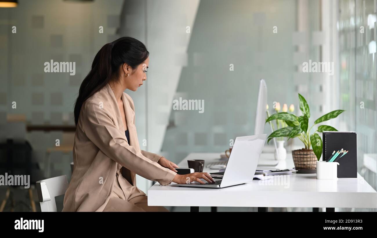 Side view of young professional female manager working on laptop at her ...