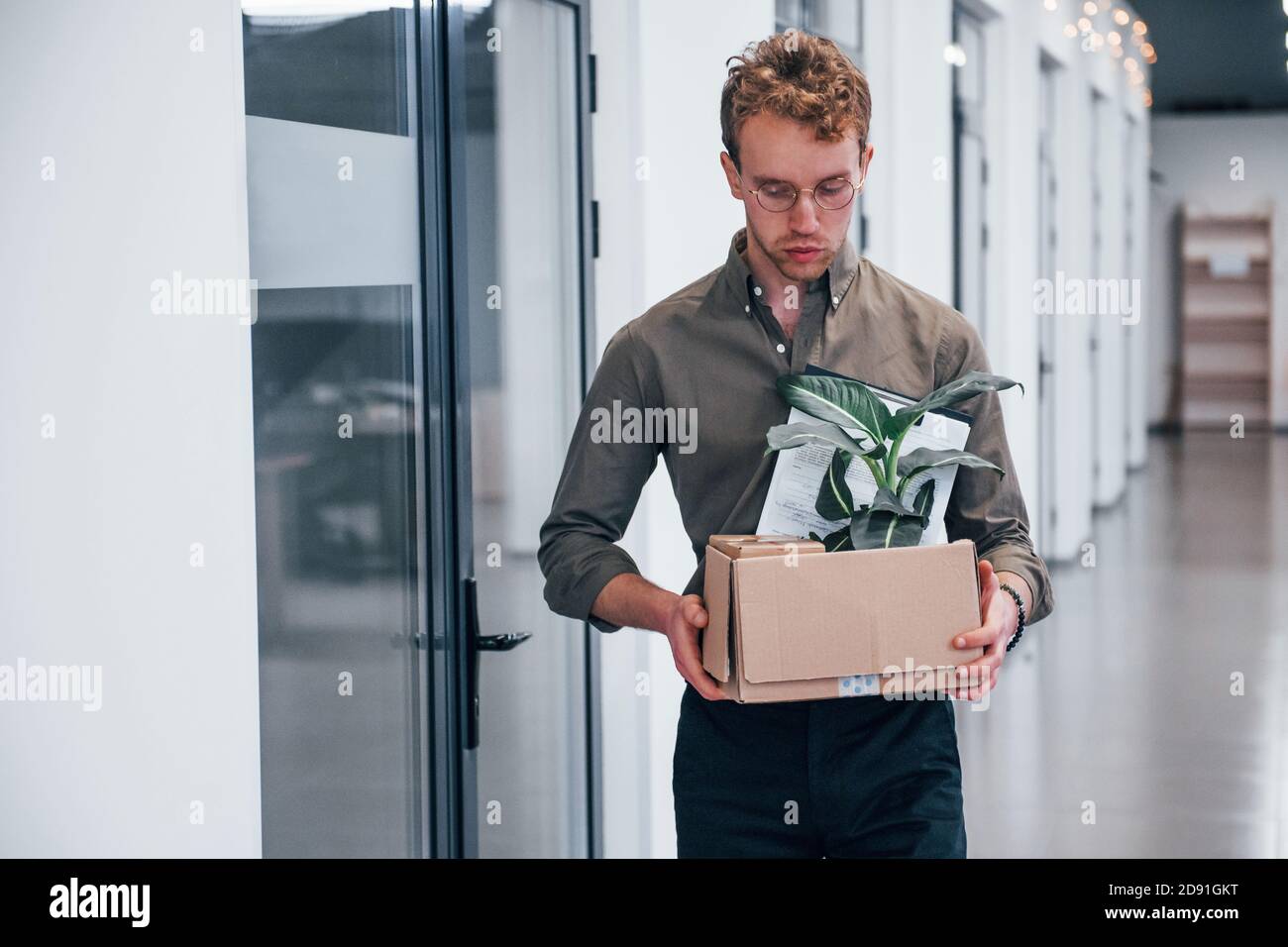 Office worker in formal wear walking with box with green plant inside ...