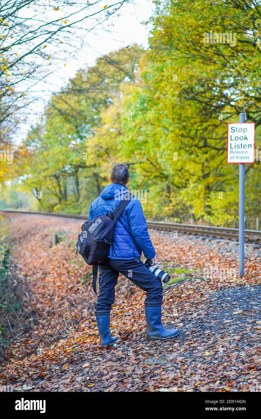 Rear view of male photographer looking down rural UK railway line at a ...