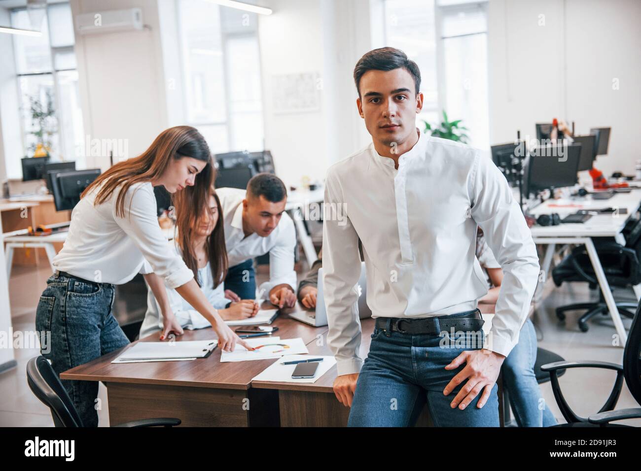 Young male employee in formal clothes standing in the office. Group of ...