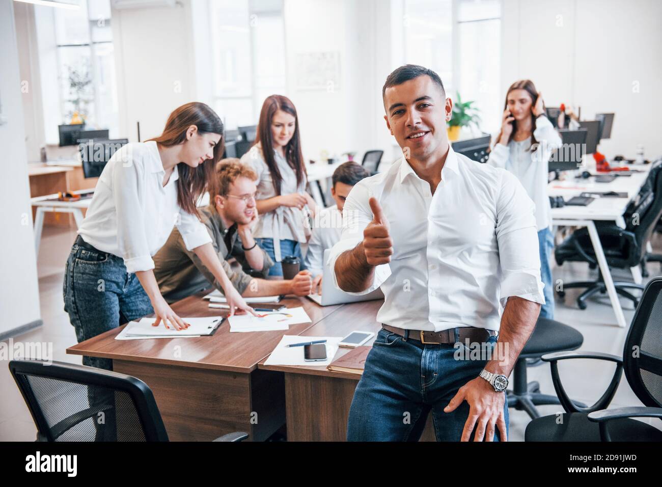 Young male employee in formal clothes standing in the office. Group of ...