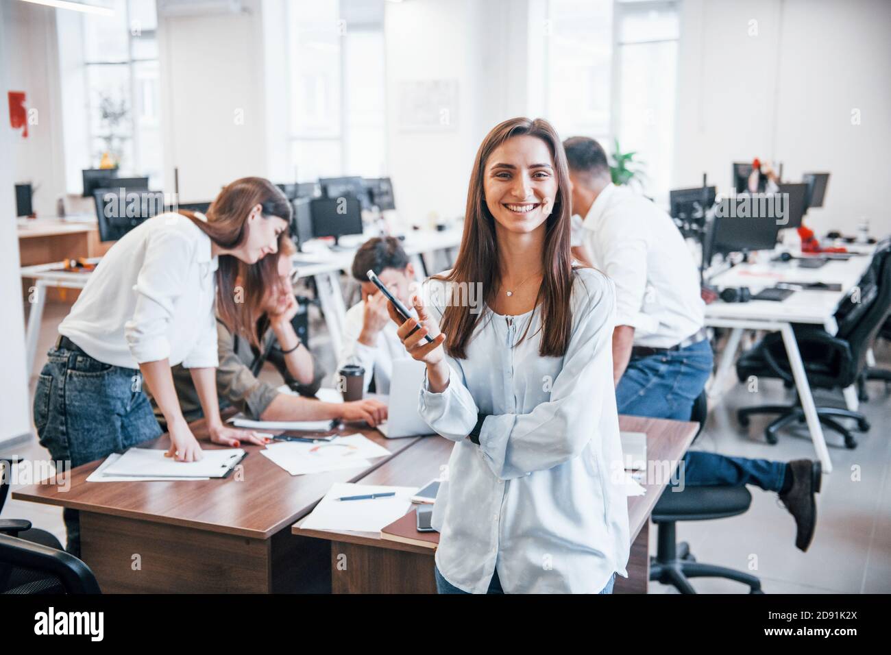 Handsome woman with phone is in the office. Group of people working at ...