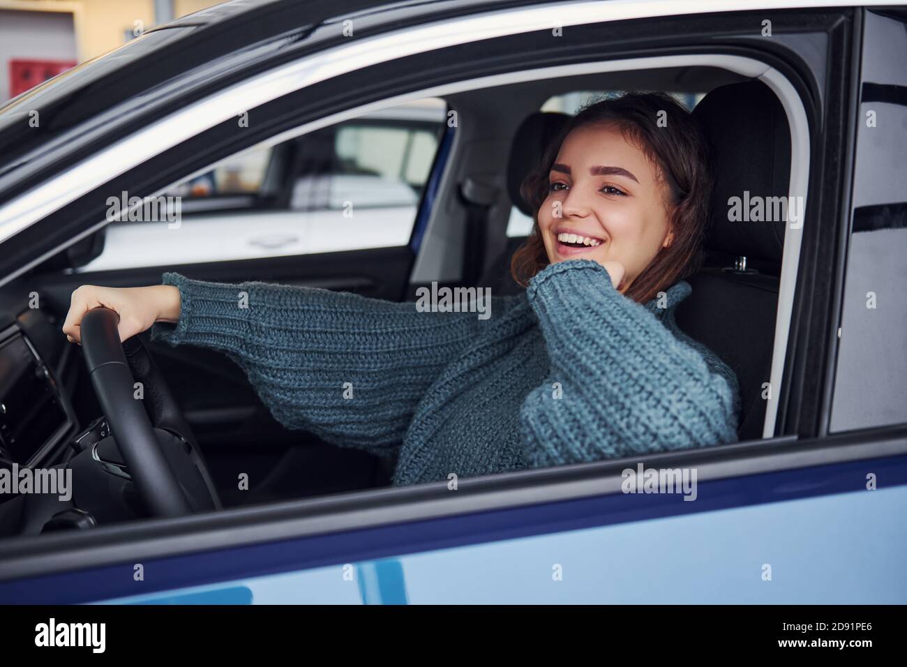 Positive young girl in casual clothes sitting inside of modern car and ...