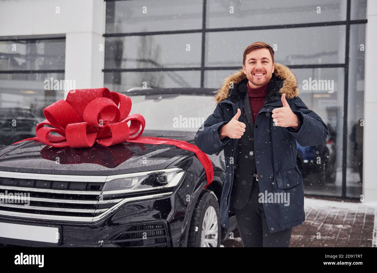 Happy owner of new modern car standing outdoors and smiling. Red gift ...