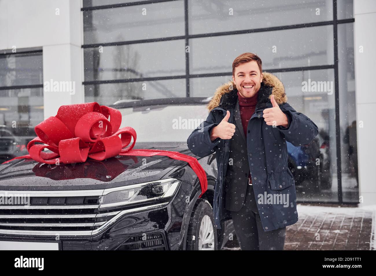Happy owner of new modern car standing outdoors and smiling. Red gift ...