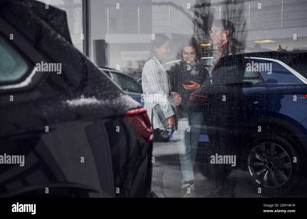 Friends standing behind glass at rainy day. Girl holds laptop in hands ...