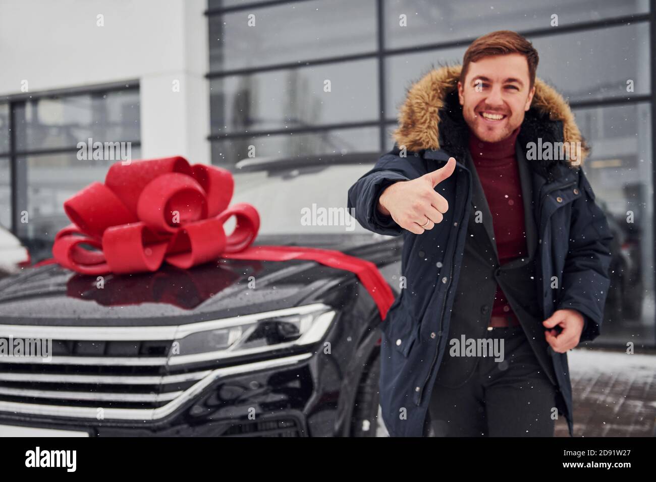 Happy owner of new modern car standing outdoors and smiling. Red gift ...