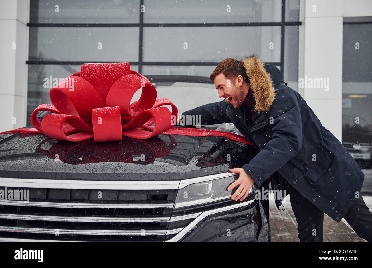 Happy owner of new modern car standing outdoors and smiling. Red gift ...