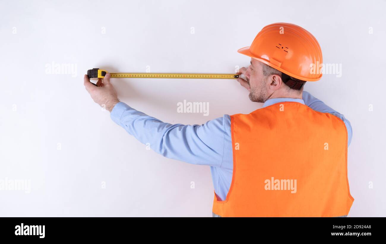 Builder Measuring Wall With Tape-Measure Standing Back To Camera ...
