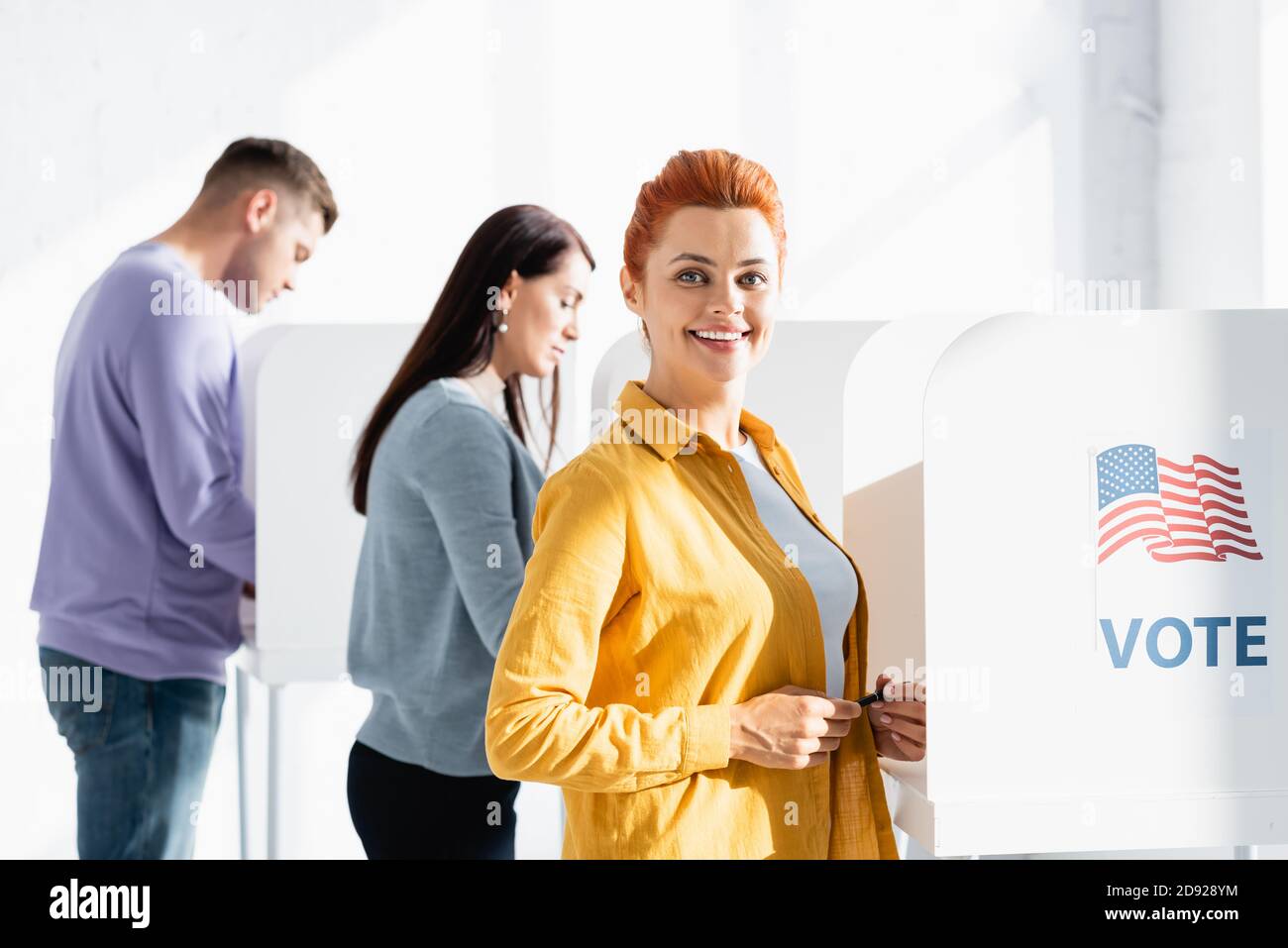 woman smiling at camera near polling booth with american flag and vote ...