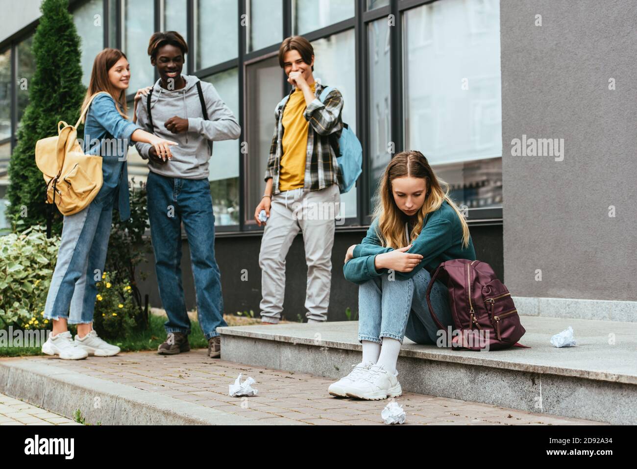 Selective focus of sad girl sitting near backpack, clumped paper and ...