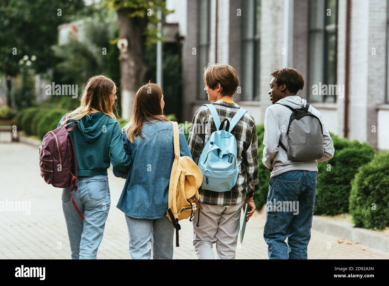 Back view of multiethnic teenagers with backpacks walking together on ...