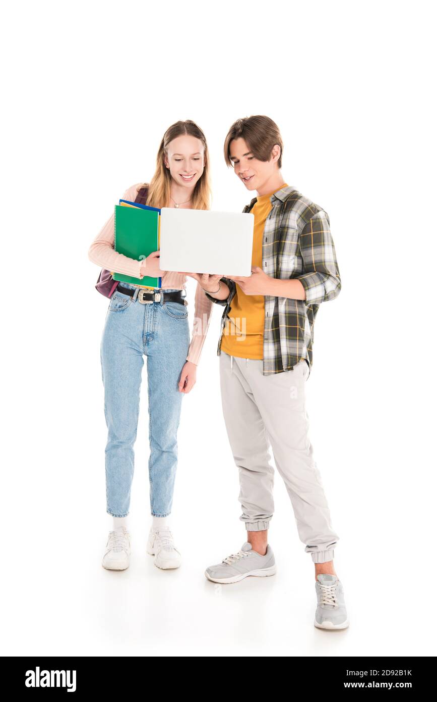 Teen boy holding laptop near friend with notebooks on white background ...