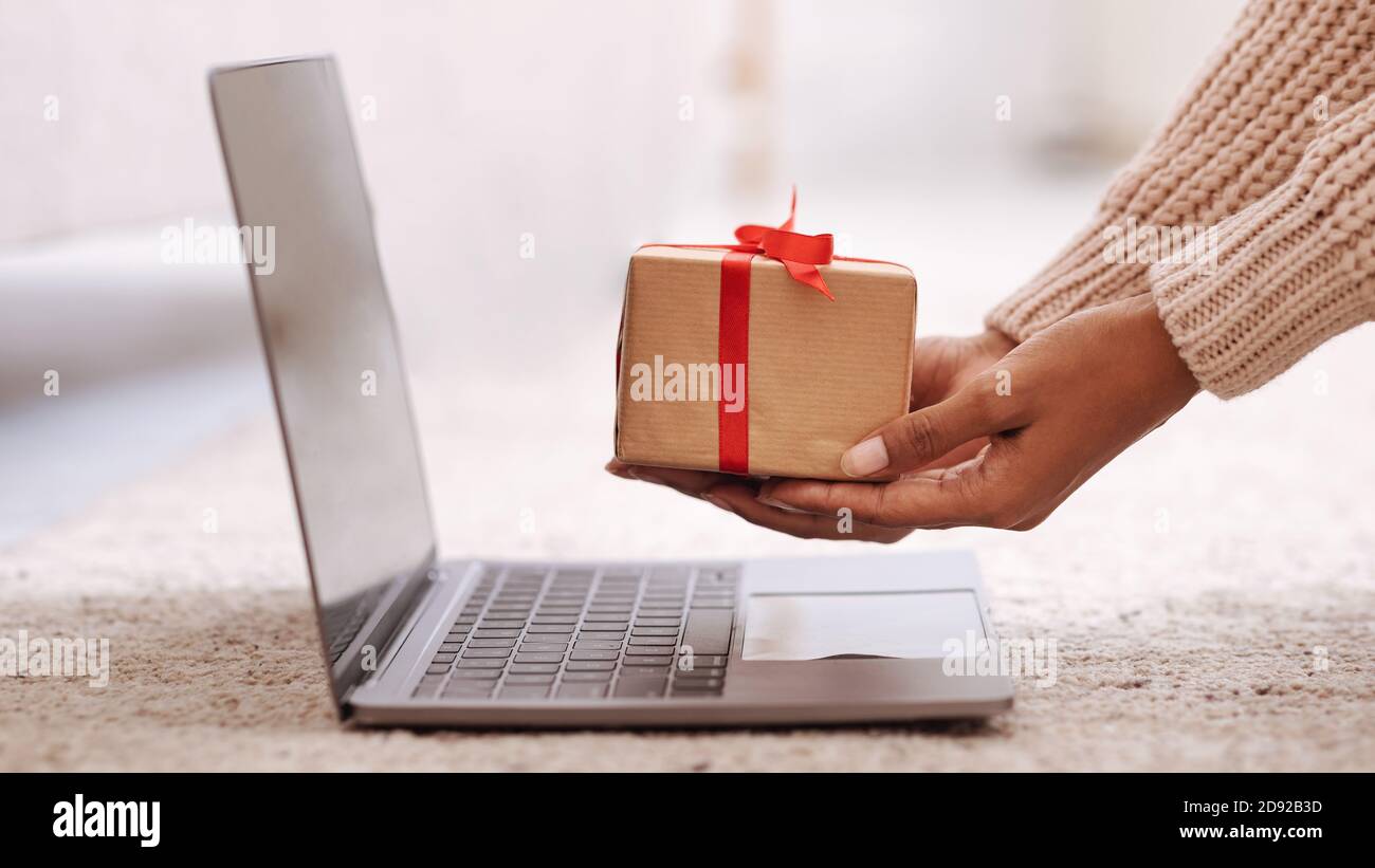 Woman showing gift box to computer screen Stock Photo - Alamy