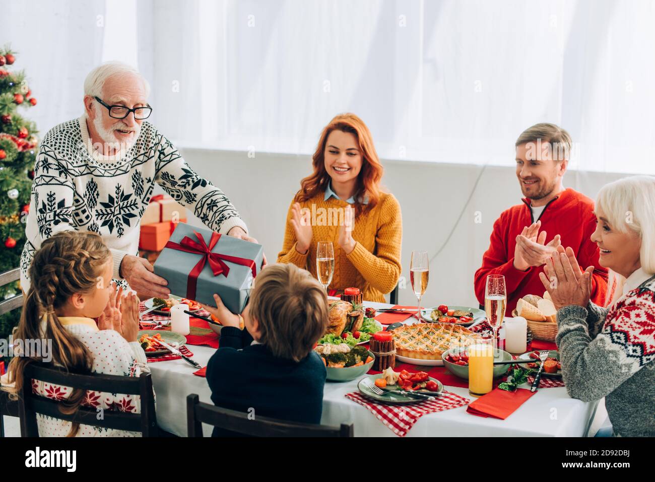 Smiling grandfather giving present to grandson near family applauding ...
