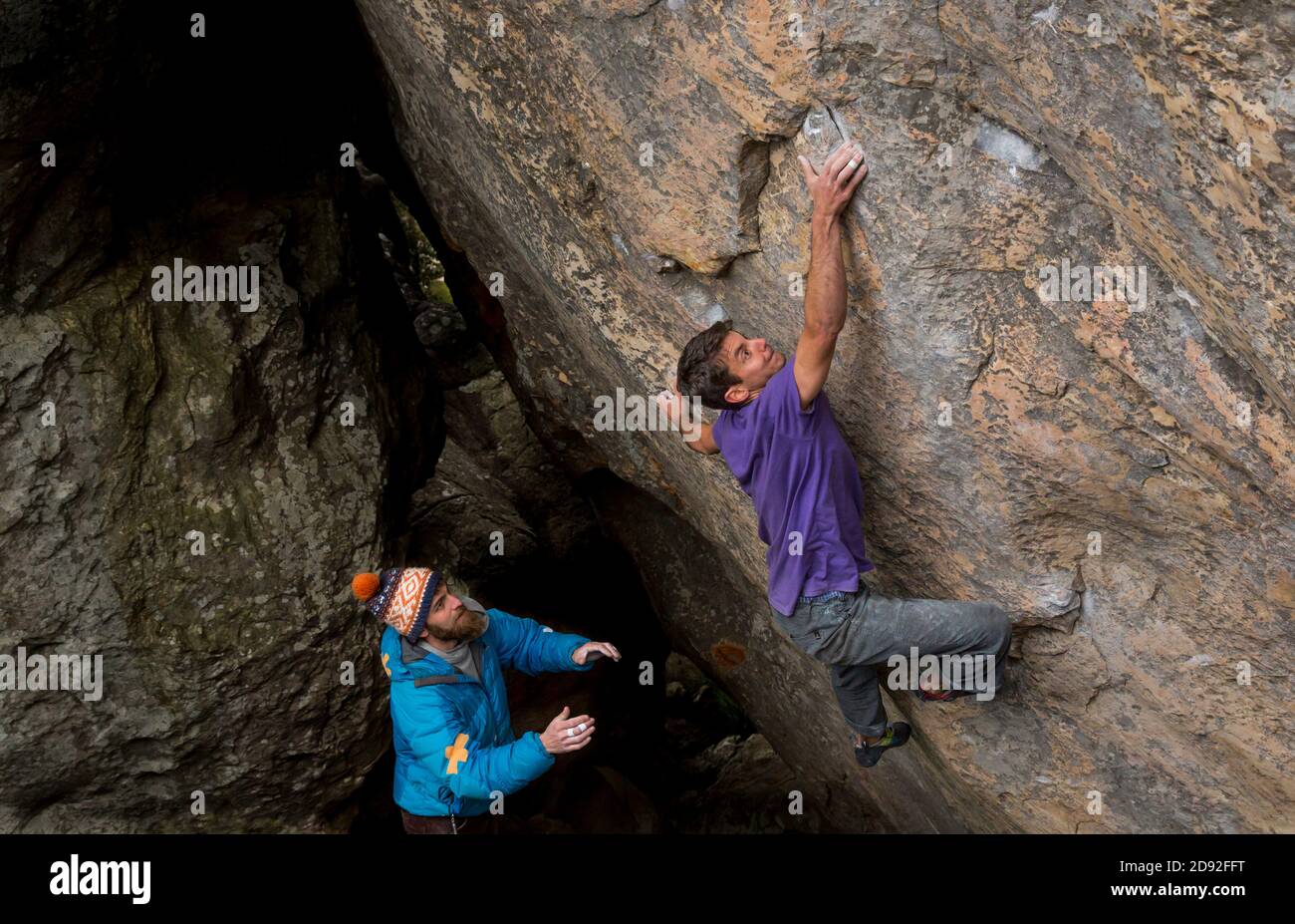 Athletic male climbs outside on a boulder with man spotting Stock Photo ...