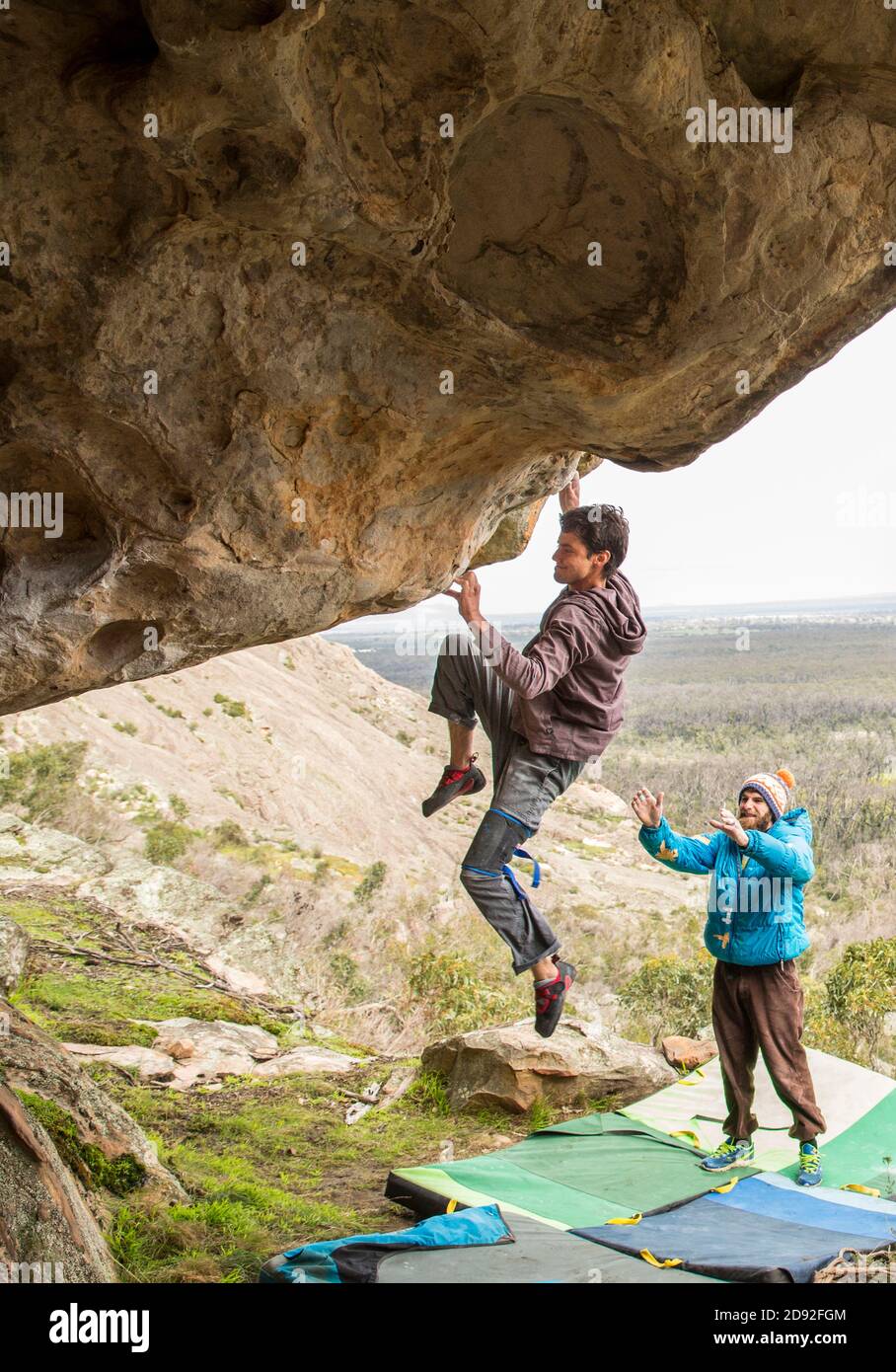 Athletic male climbs outside on a boulder with man spotting Stock Photo ...