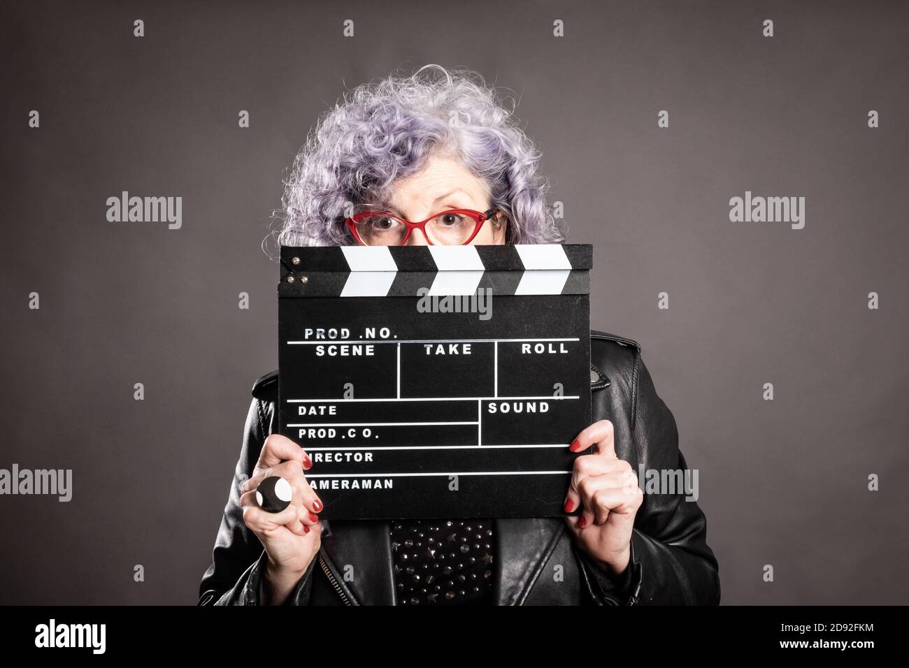 Close up portrait of beautiful older woman holding a movie clapper on a ...
