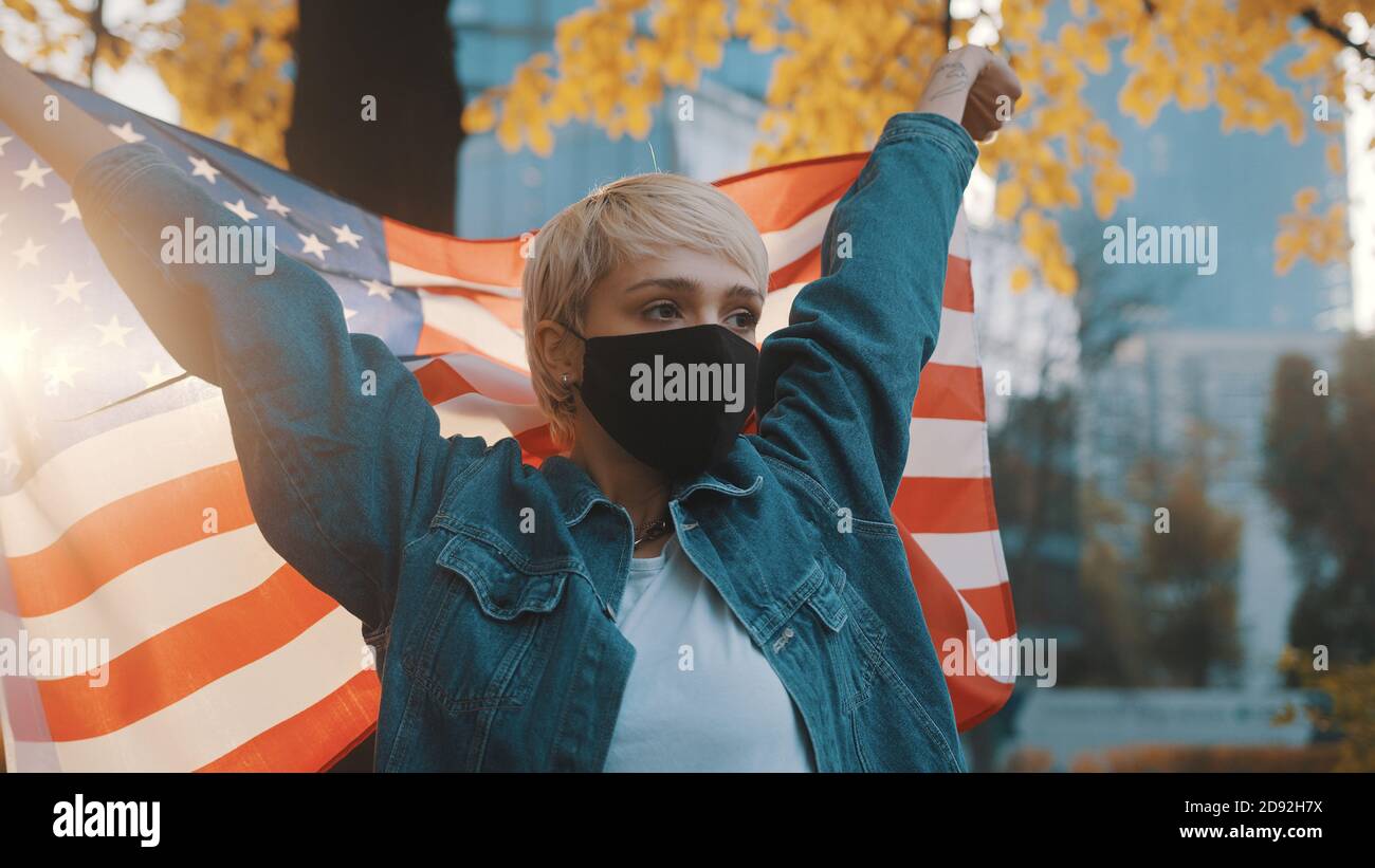 Young woman with face mask proudly holding american flag outdoors.USA ...