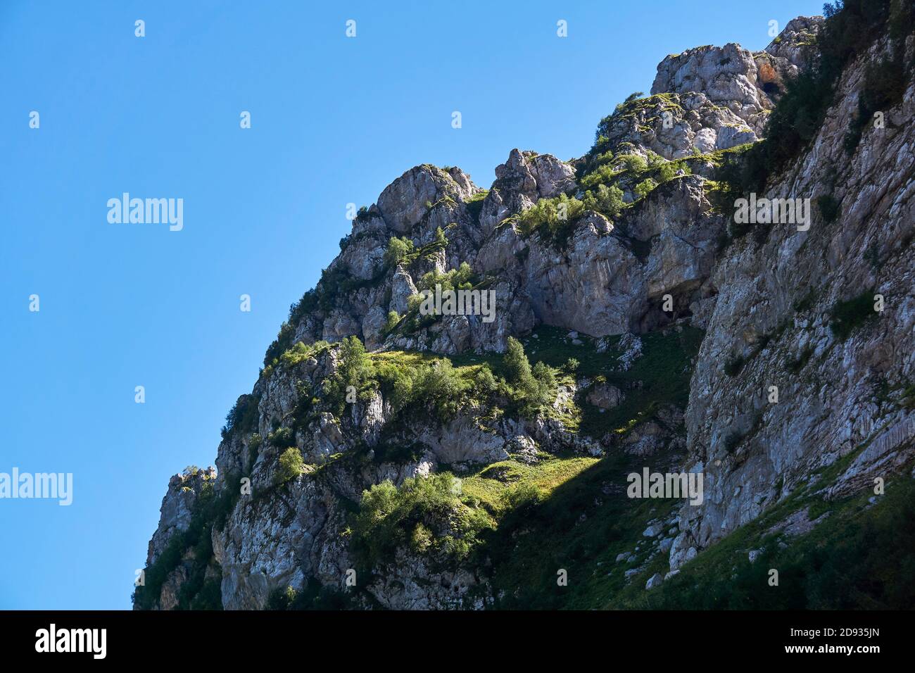 steep mountain ledges overgrown with vegetation, against the background ...