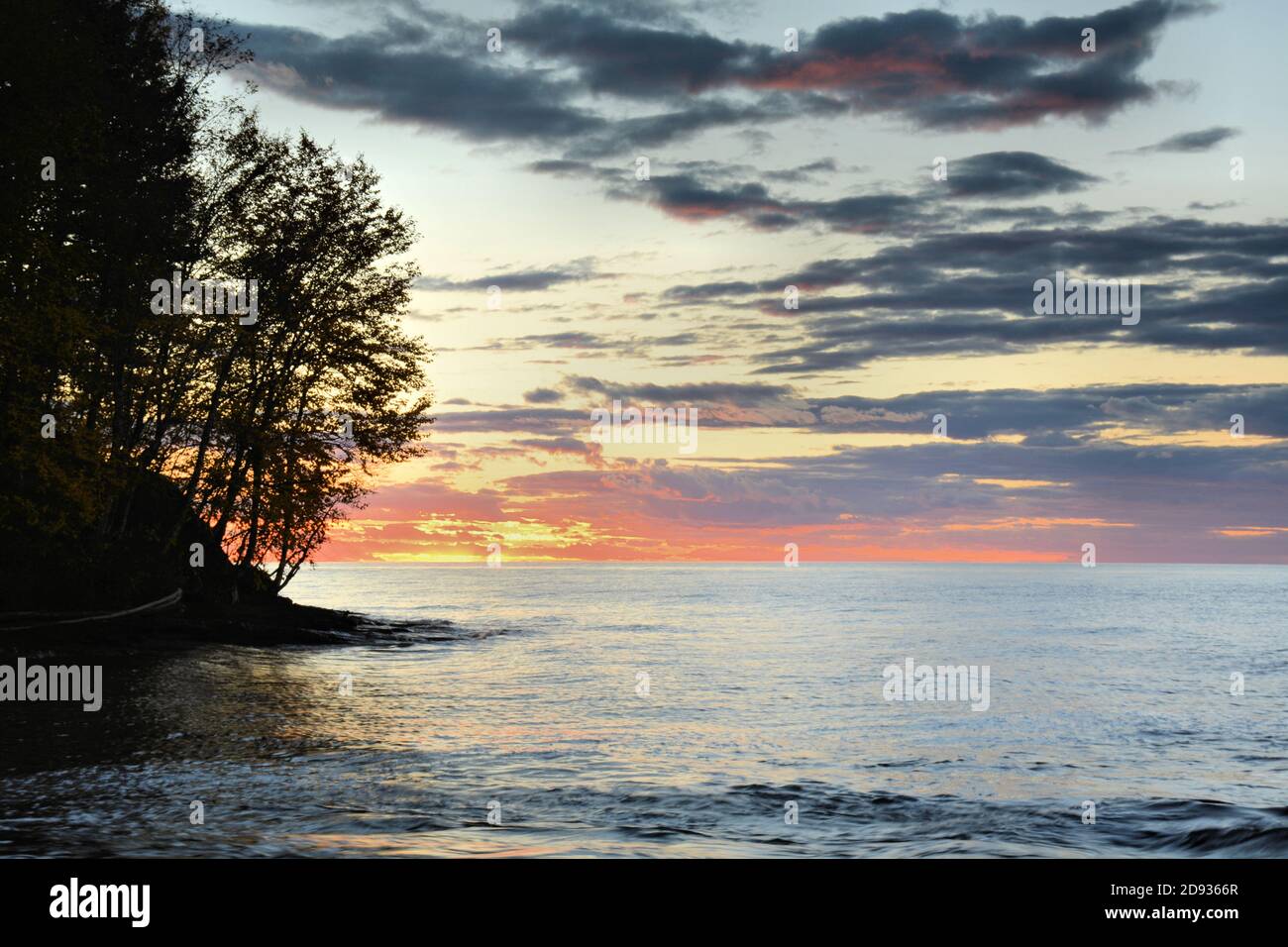 A brilliant sunset sets clouds aflame over the peaceful waters of Lake ...