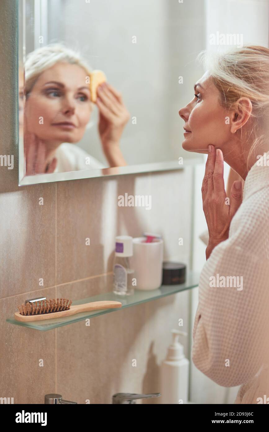 Mirror reflection of smiling middle aged caucasian woman using collagen ...