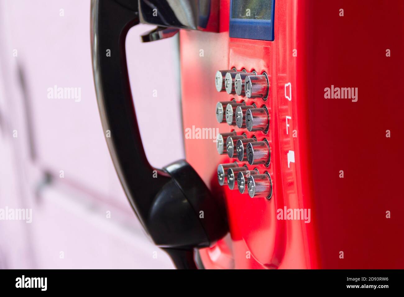 Red street payphone with round stainless steel buttons close-up. An ...
