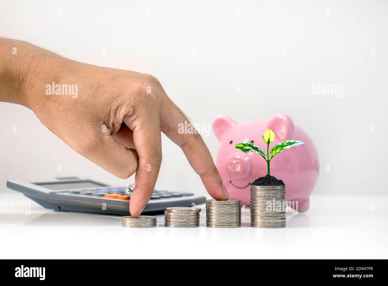 The male investor's hand rests on a pile of flat coins leap and trees ...