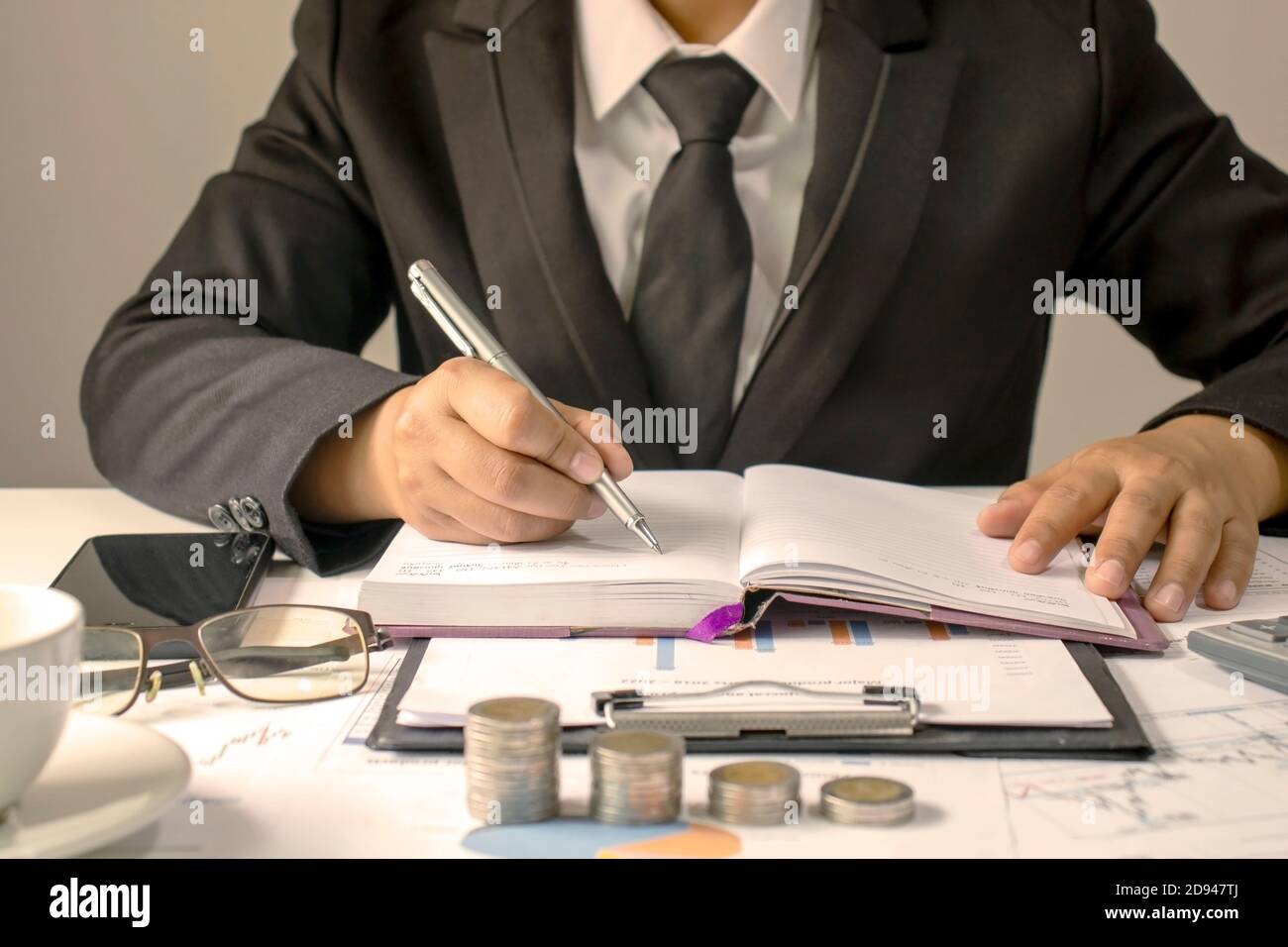 Close-up of a man writing financial notes on his desk, including ...