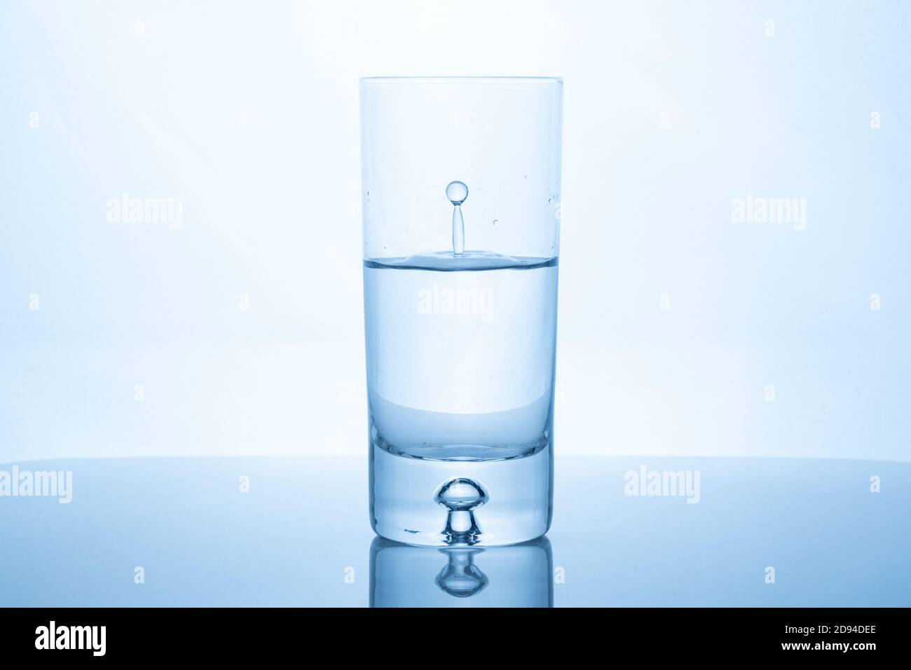 Water drop splash inside glass half full against bright background ...