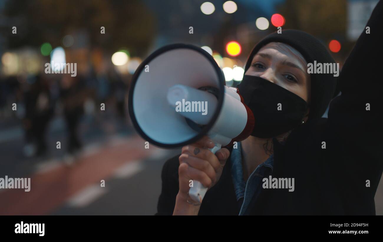 young woman with face mask shouting slogans to loudspeaker at street ...