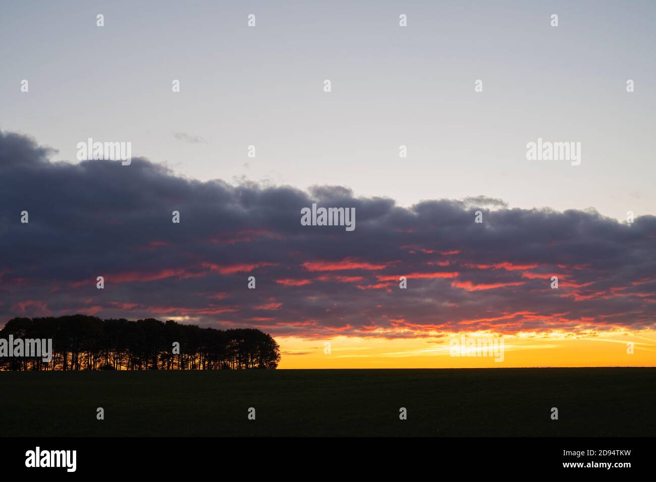 Band of rain clouds at sunset over the cotswold countryside with trees ...