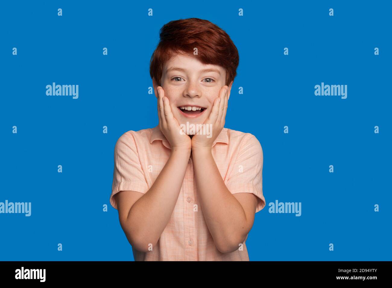 Shocked caucasian boy is touching his face while looking at camera and ...